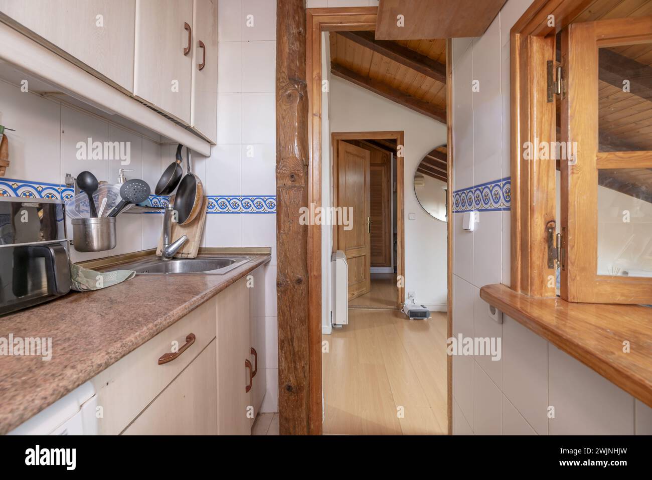 A small kitchen with wooden furniture and a serving hatch with a window ...