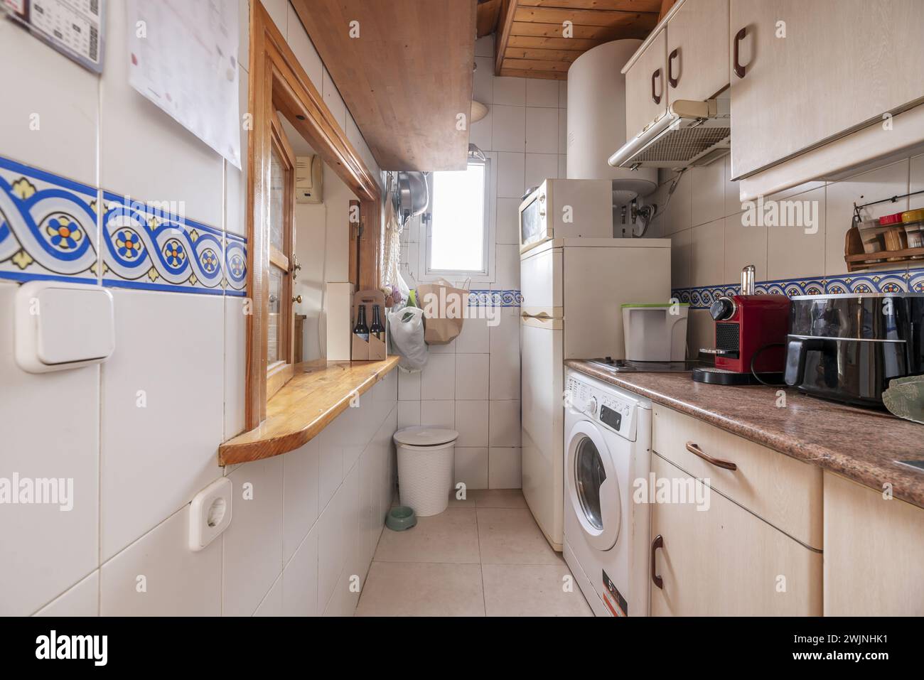 A small kitchen with wooden furniture, a serving hatch with a window to ...