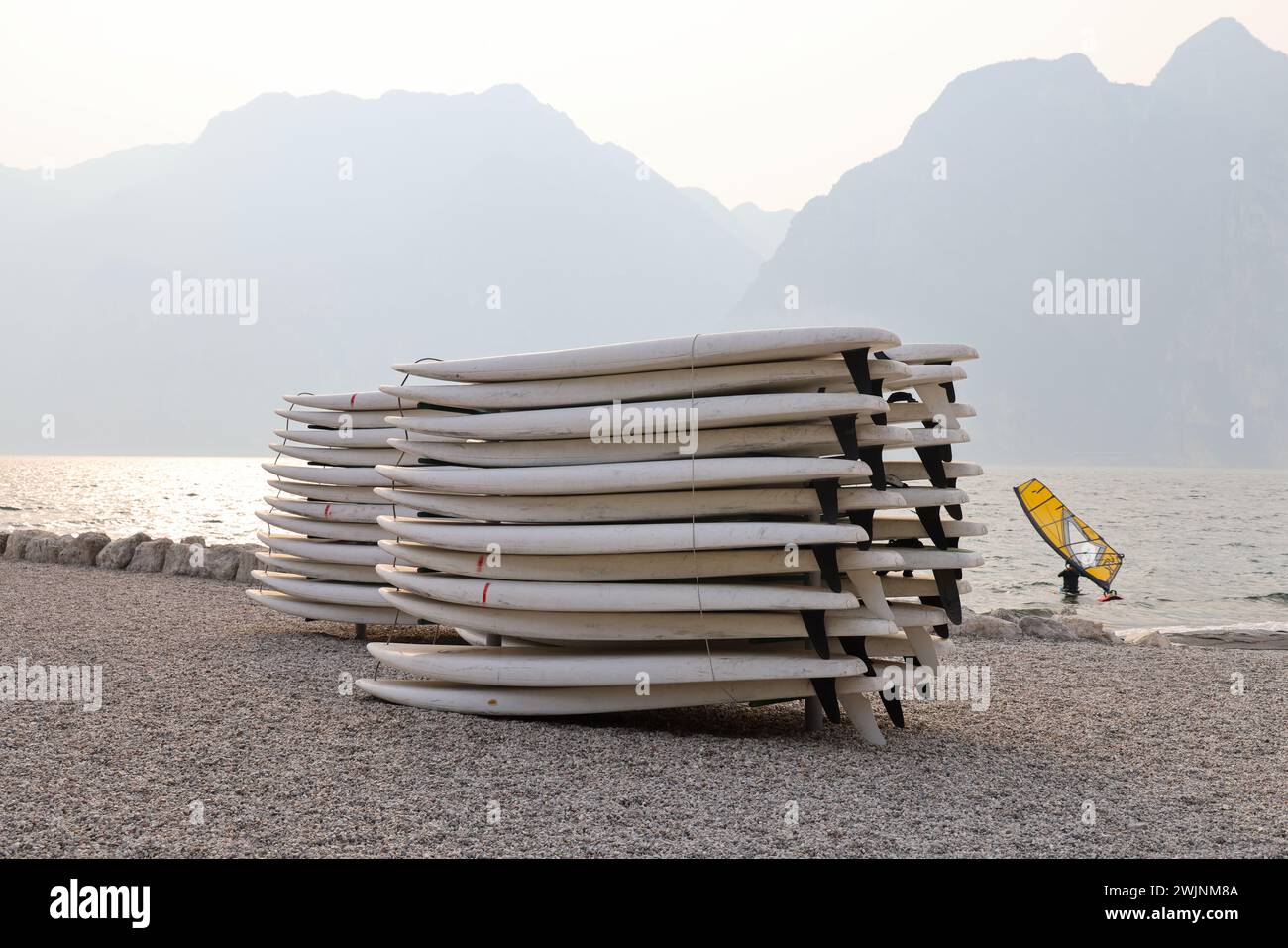 Stack up white paddle boards on a shore of lake Garda on a foggy day ...