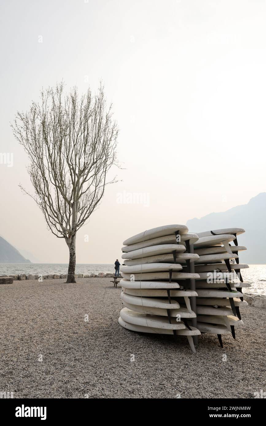 Stack up white paddle boards on a shore of lake Garda on a foggy day ...