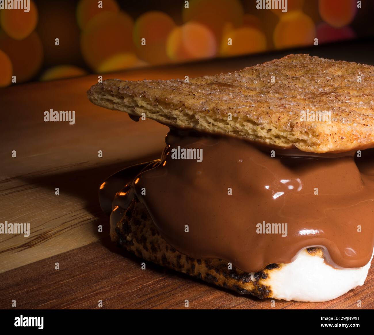 Smore on a wood table with chocolate melting and orange party lights ...