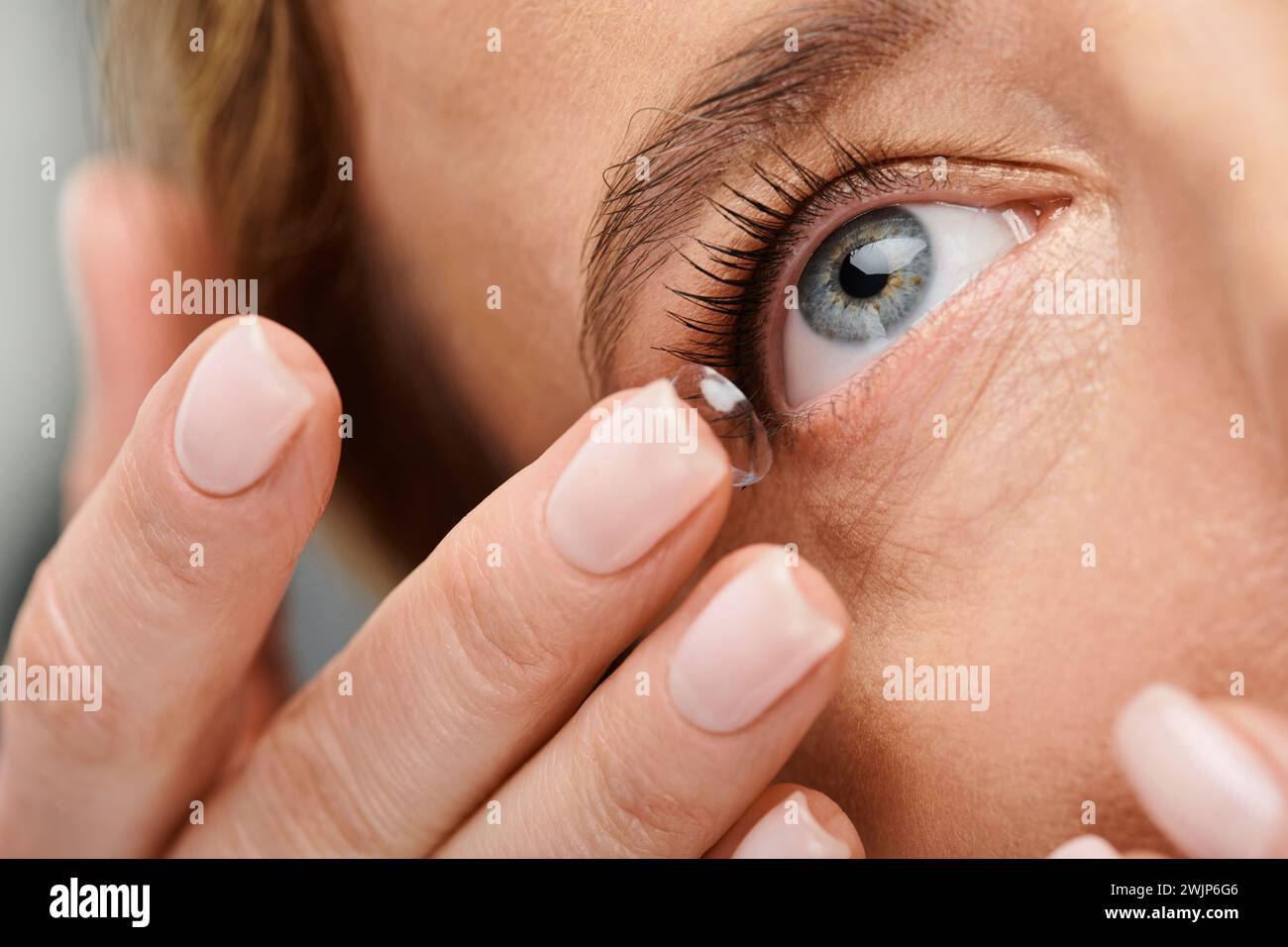 close up of good looking woman wearing carefully her contact lens while ...