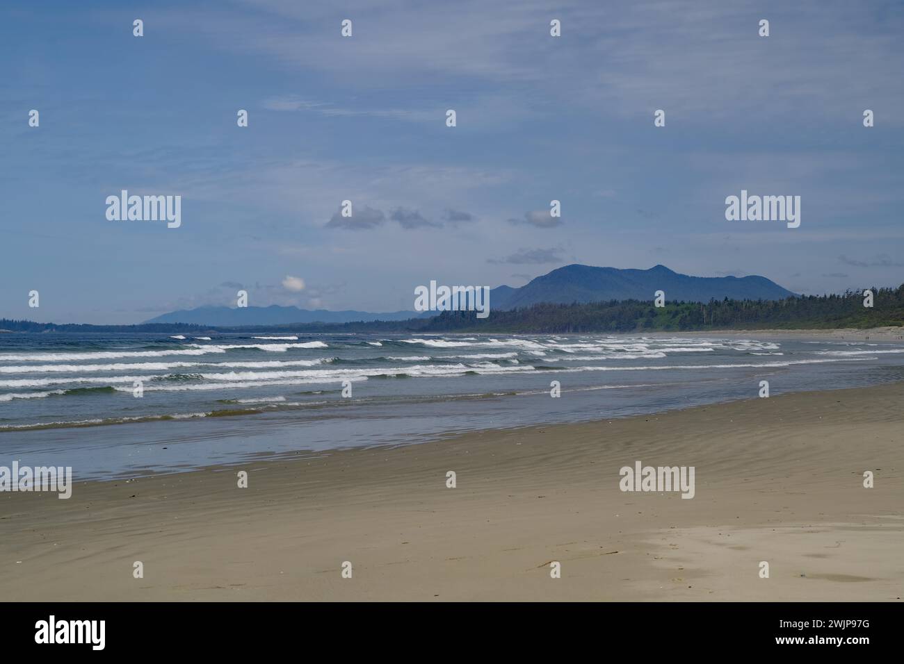 Endless empty sandy beach with swell and mountains in the background ...