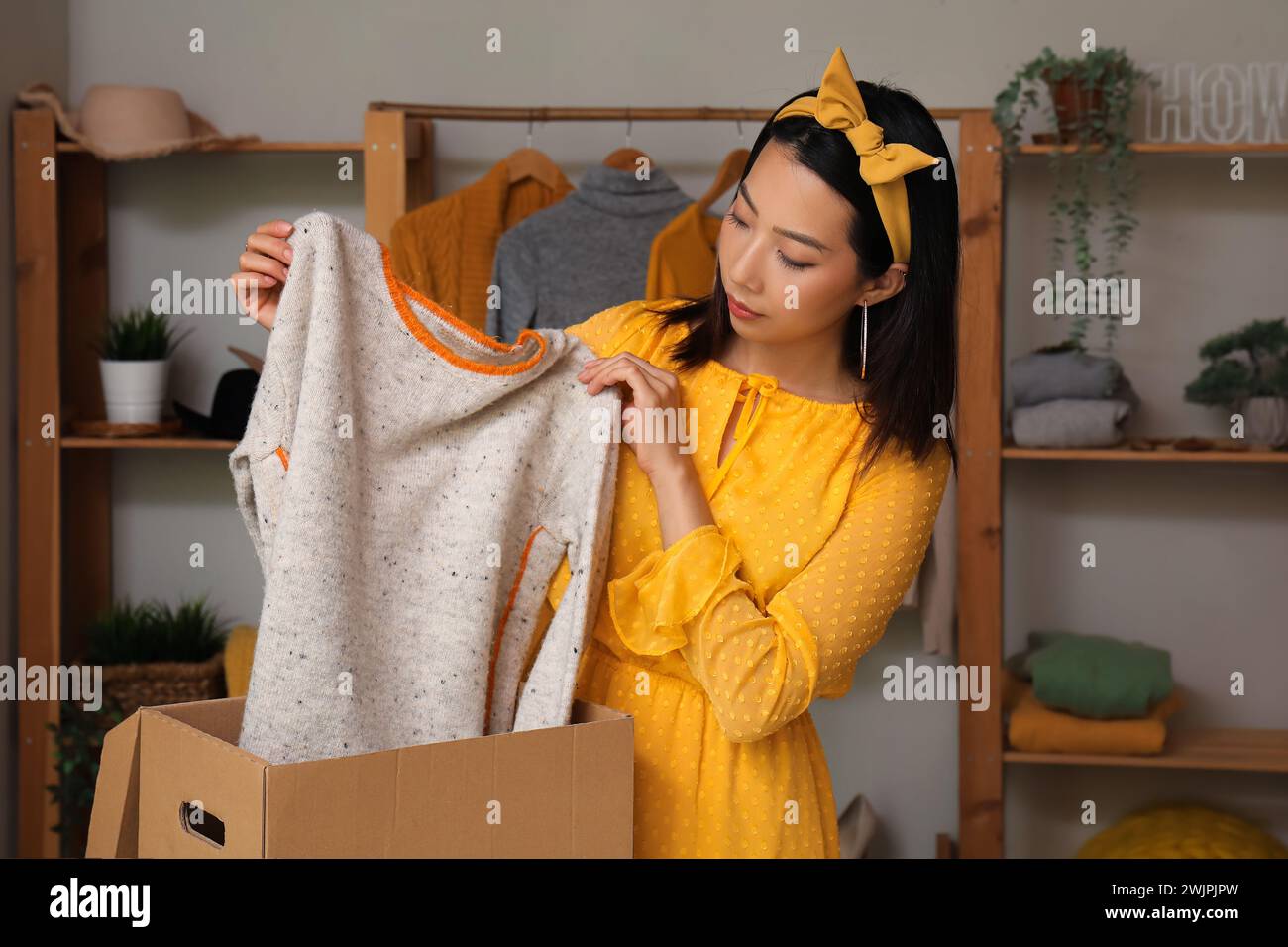Beautiful young woman with clean sweater in laundry room Stock Photo ...