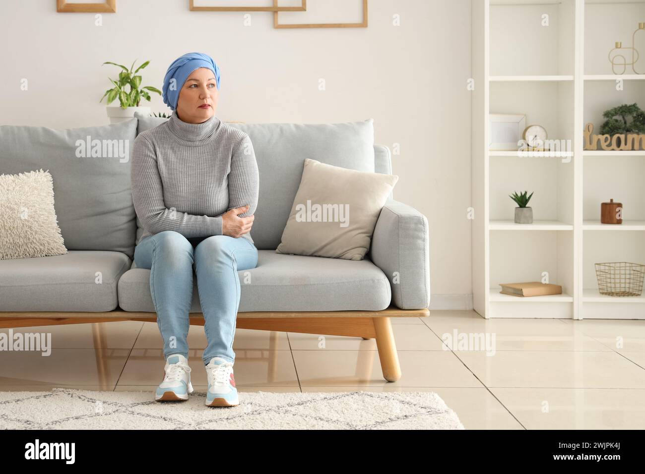 Mature woman after chemotherapy sitting on sofa at home. Stomach cancer ...