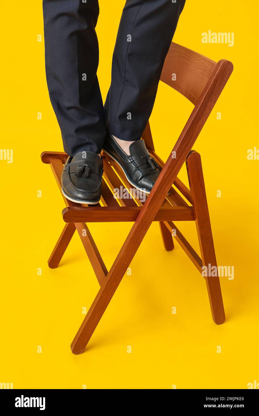 Legs of young man in black stylish shoes on chair against yellow ...