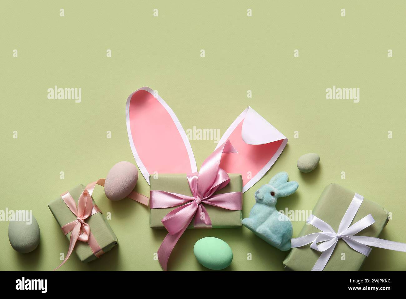 Paper bunny ears with Easter eggs and gift boxes on green background ...