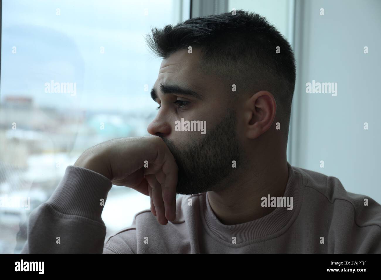 Portrait of sad man near window at home Stock Photo - Alamy