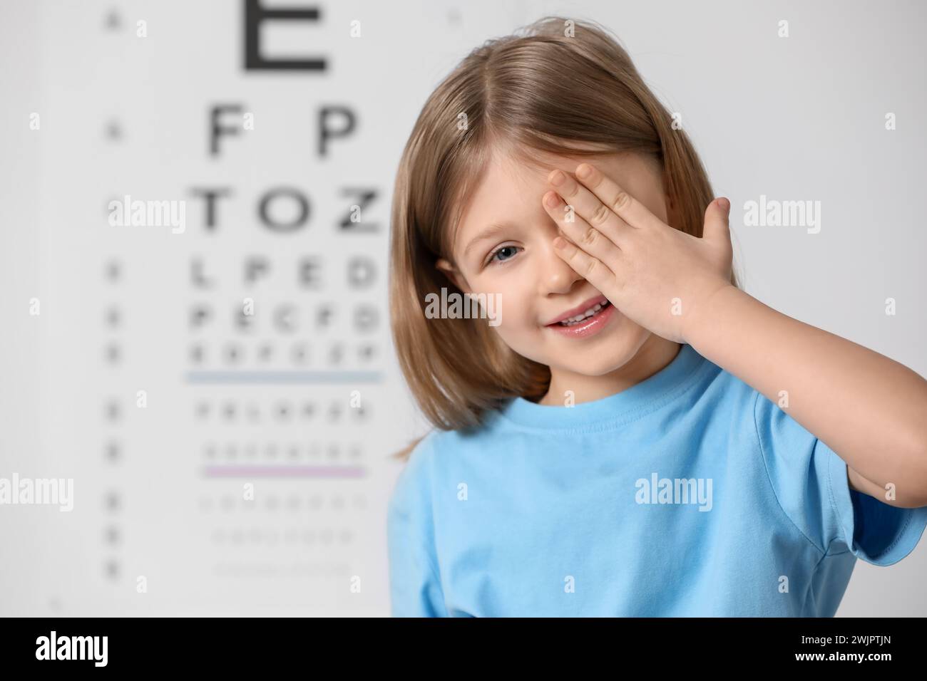 Little girl covering her eye against vision test chart Stock Photo - Alamy