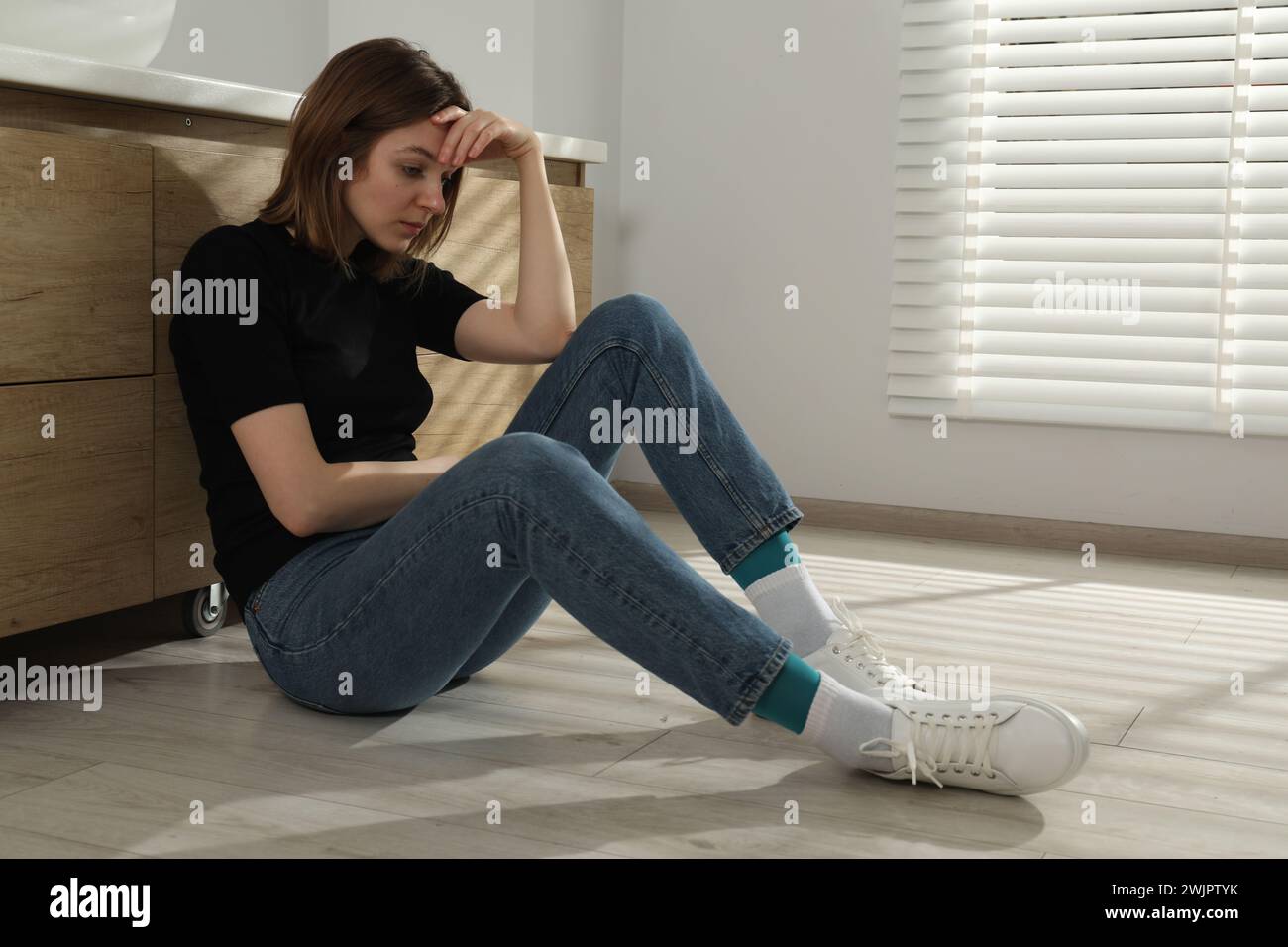 Sad young woman sitting on floor in bathroom, space for text Stock ...
