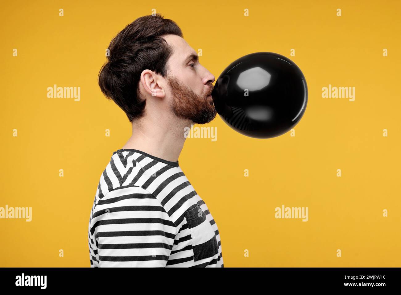 Man inflating black balloon on yellow background Stock Photo - Alamy