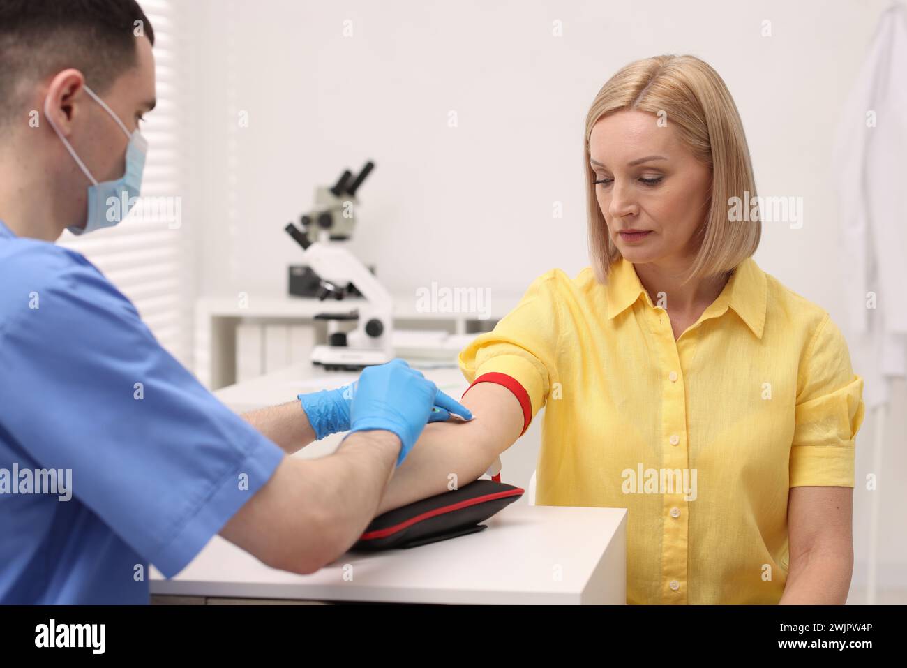 Doctor taking blood sample from patient with syringe at white table in ...