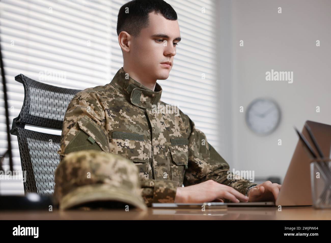 Military service. Young soldier working with laptop at table in office ...