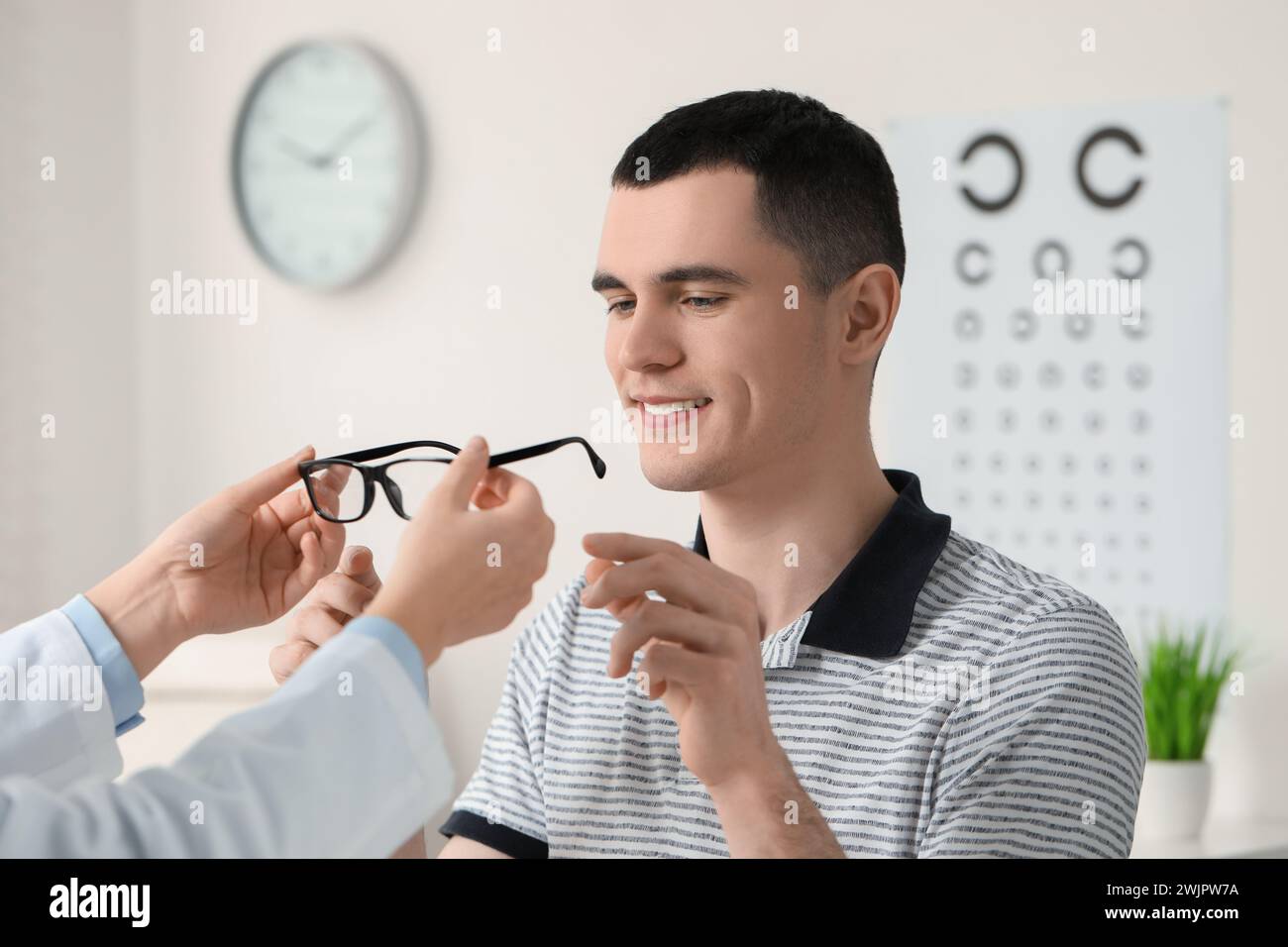 Vision testing. Ophthalmologist giving glasses to young man indoors ...
