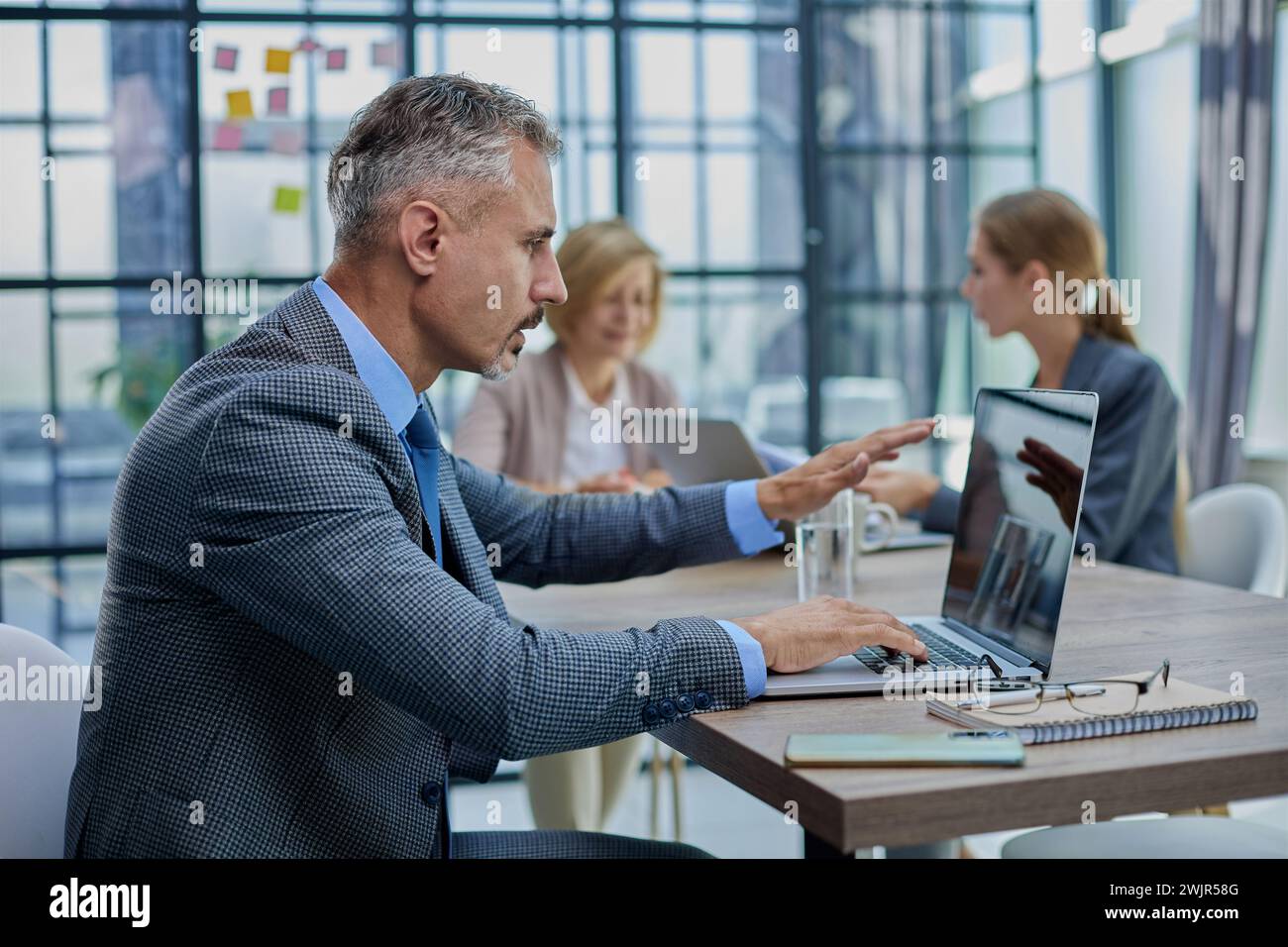 Confident businessman sitting at conference table in modern office ...