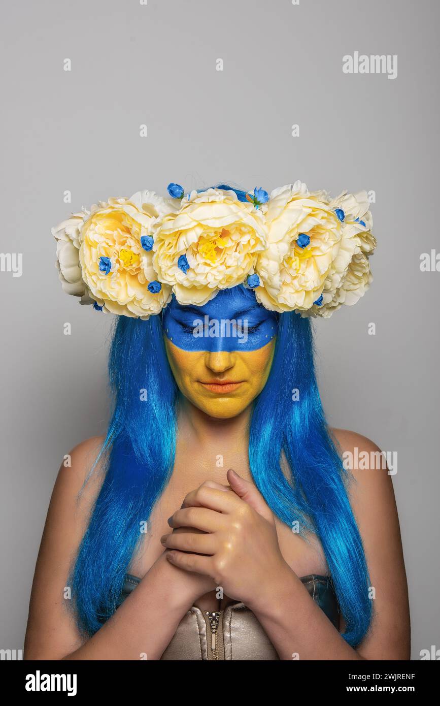 Young woman with yellow blue face art, wreath of peonies on head ...