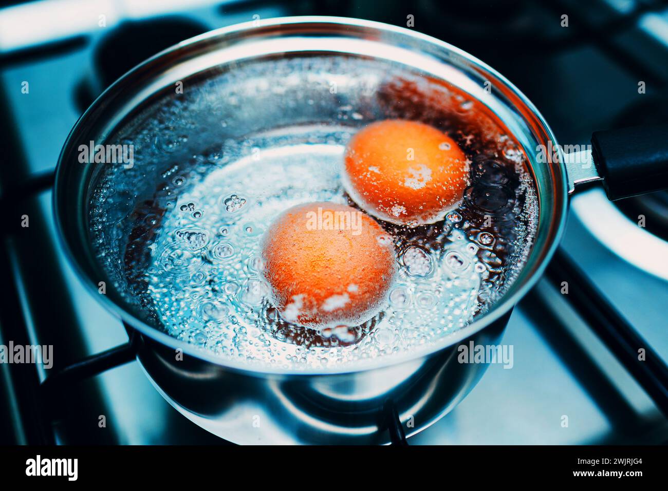 Stainless steel saucepan with boiling eggs for breakfast in boiling water on gas stove top view ...