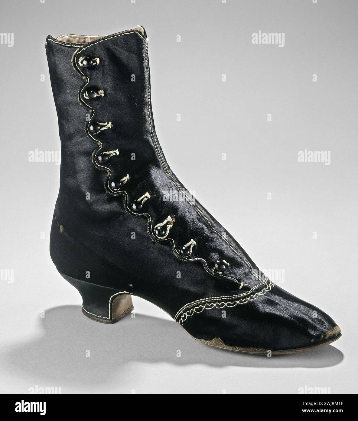 Right foot boot in black satin with white wire stitching, closing on ...