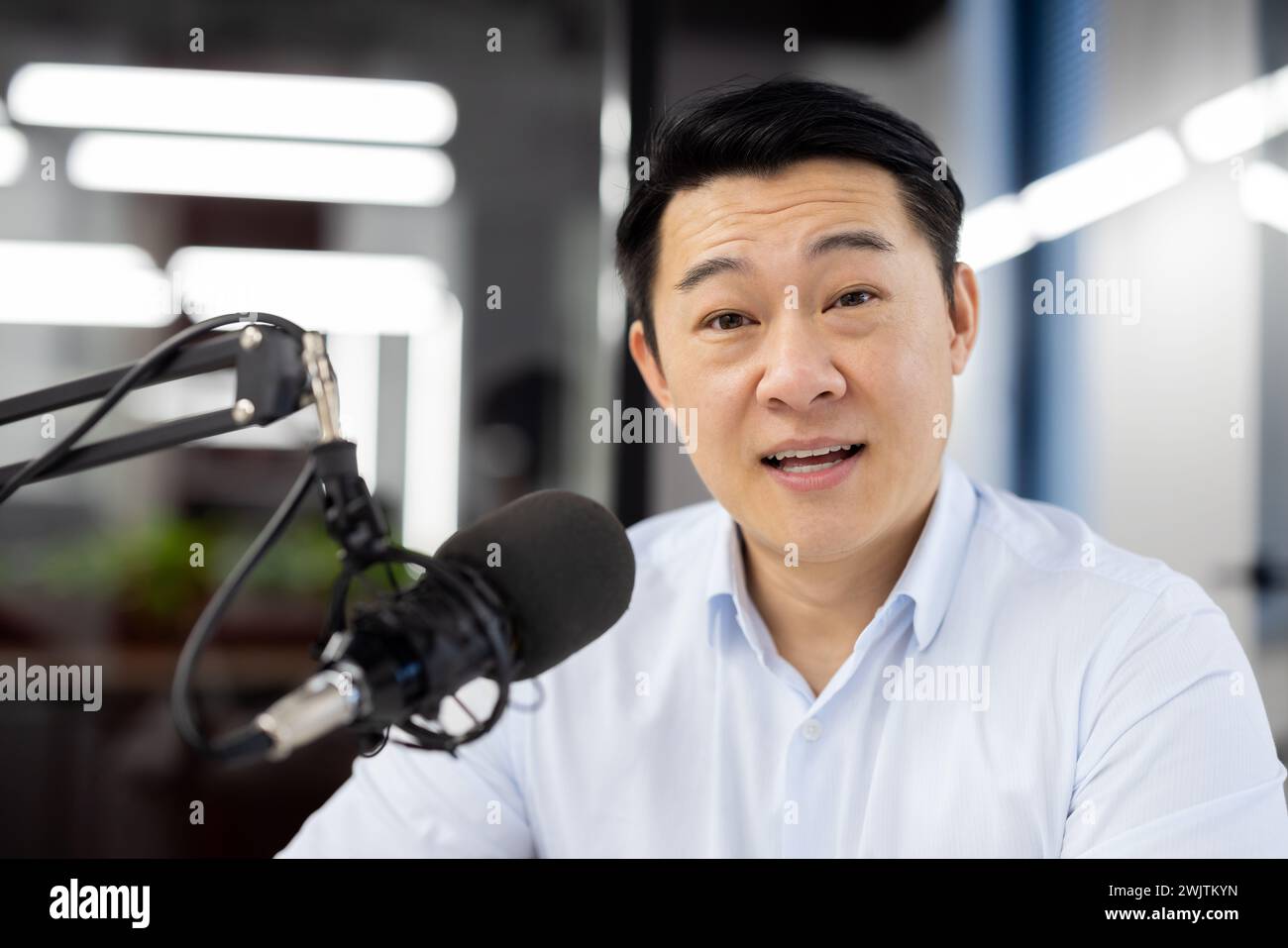 Asian male broadcaster speaking into microphone in a professional ...