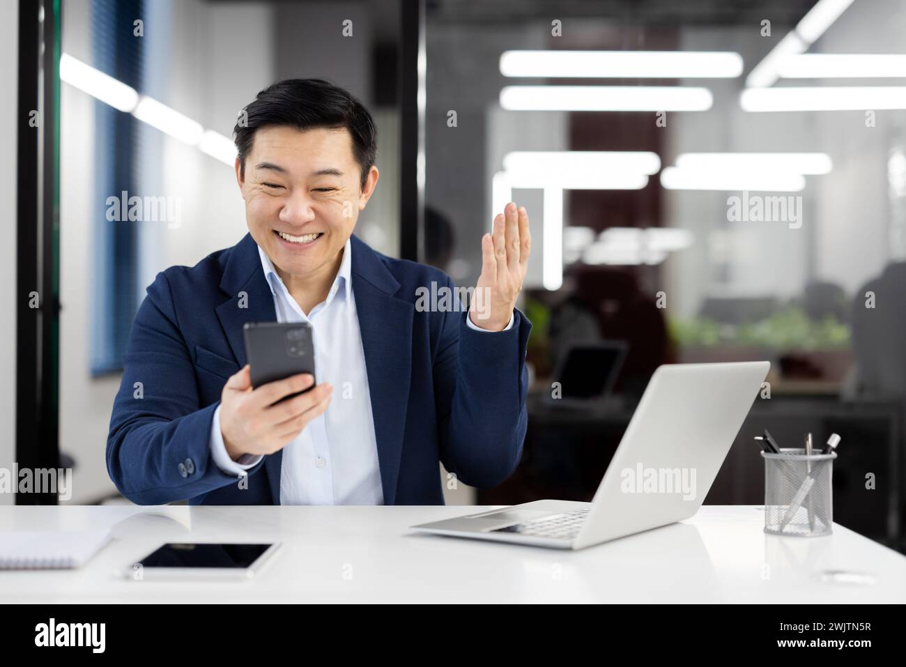 Happy Asian executive engaging in a virtual greeting, waving at the ...