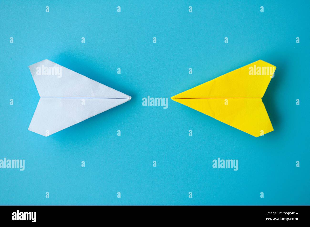 Top view of a white and yellow paper airplanes origami flying towards each other on blue ...