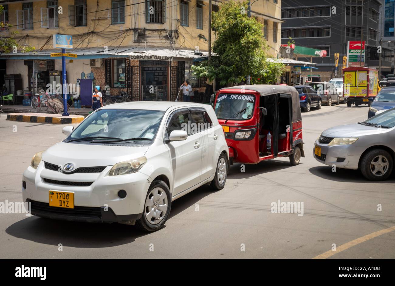 Modern cars and a bajaji or tuk tuk driving in a street in central Dar ...