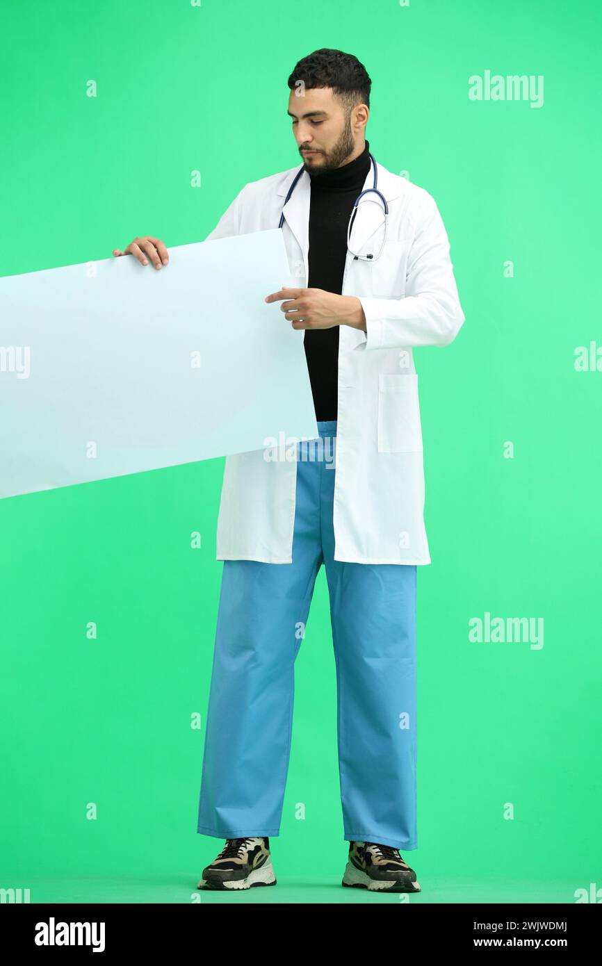 The doctor, in full height, on a green background, shows a white sheet ...
