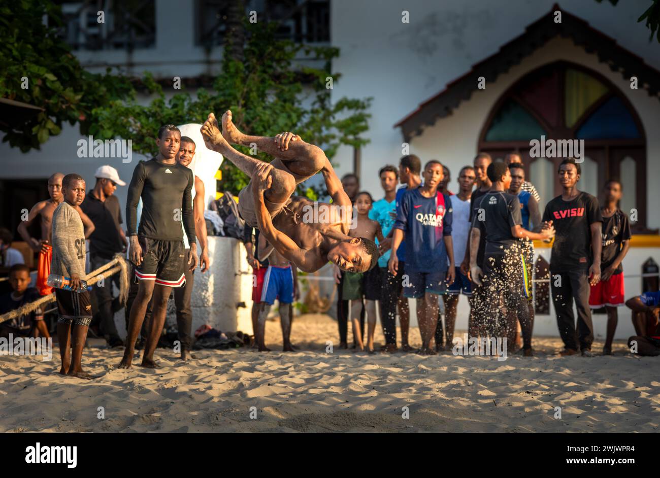 A young man performs acrobatics in the late afternoon on the beach in ...