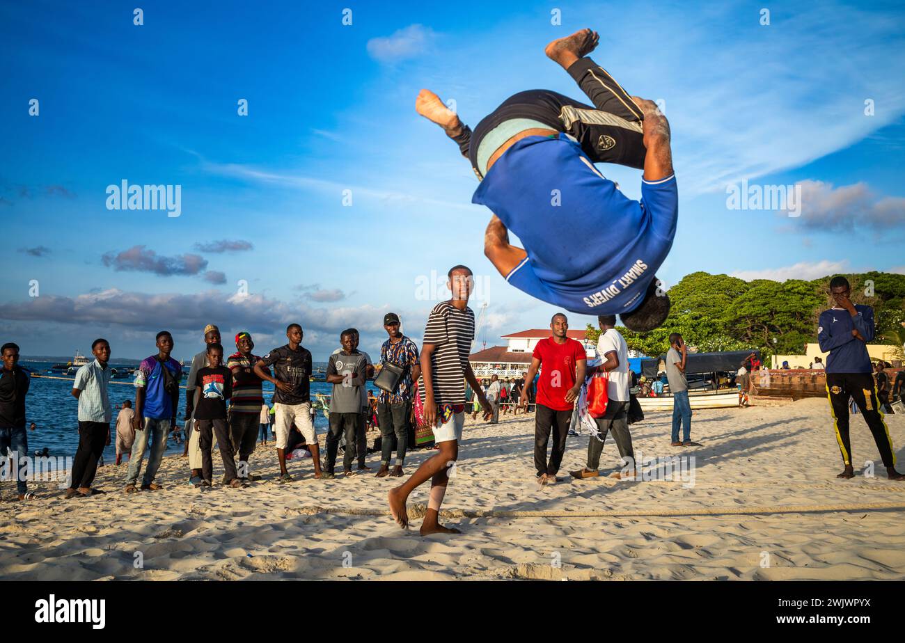 A young man performs acrobatics in the late afternoon on the beach in ...