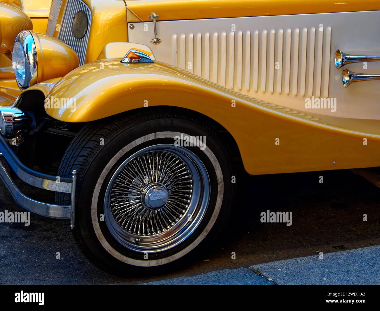 The image captures a shiny wire-spoke wheel of a classic yellow car ...