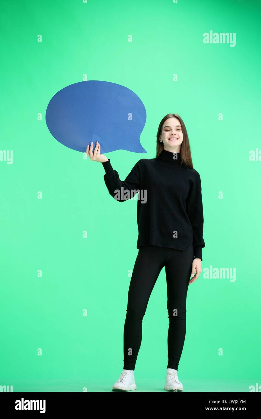 A woman, full-length, on a green background, shows a blue comment sign ...