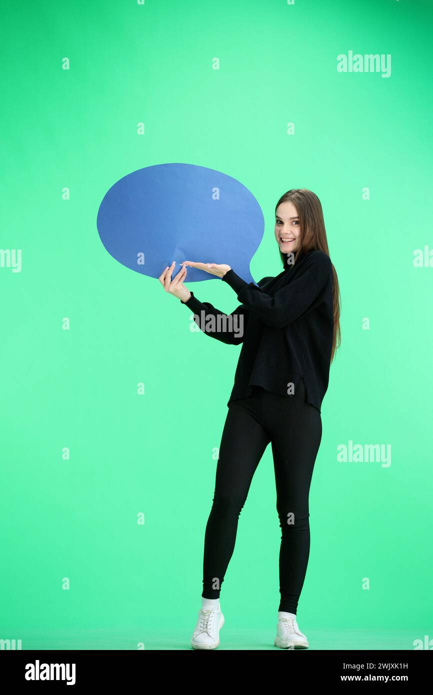 A woman, full-length, on a green background, shows a blue comment sign ...