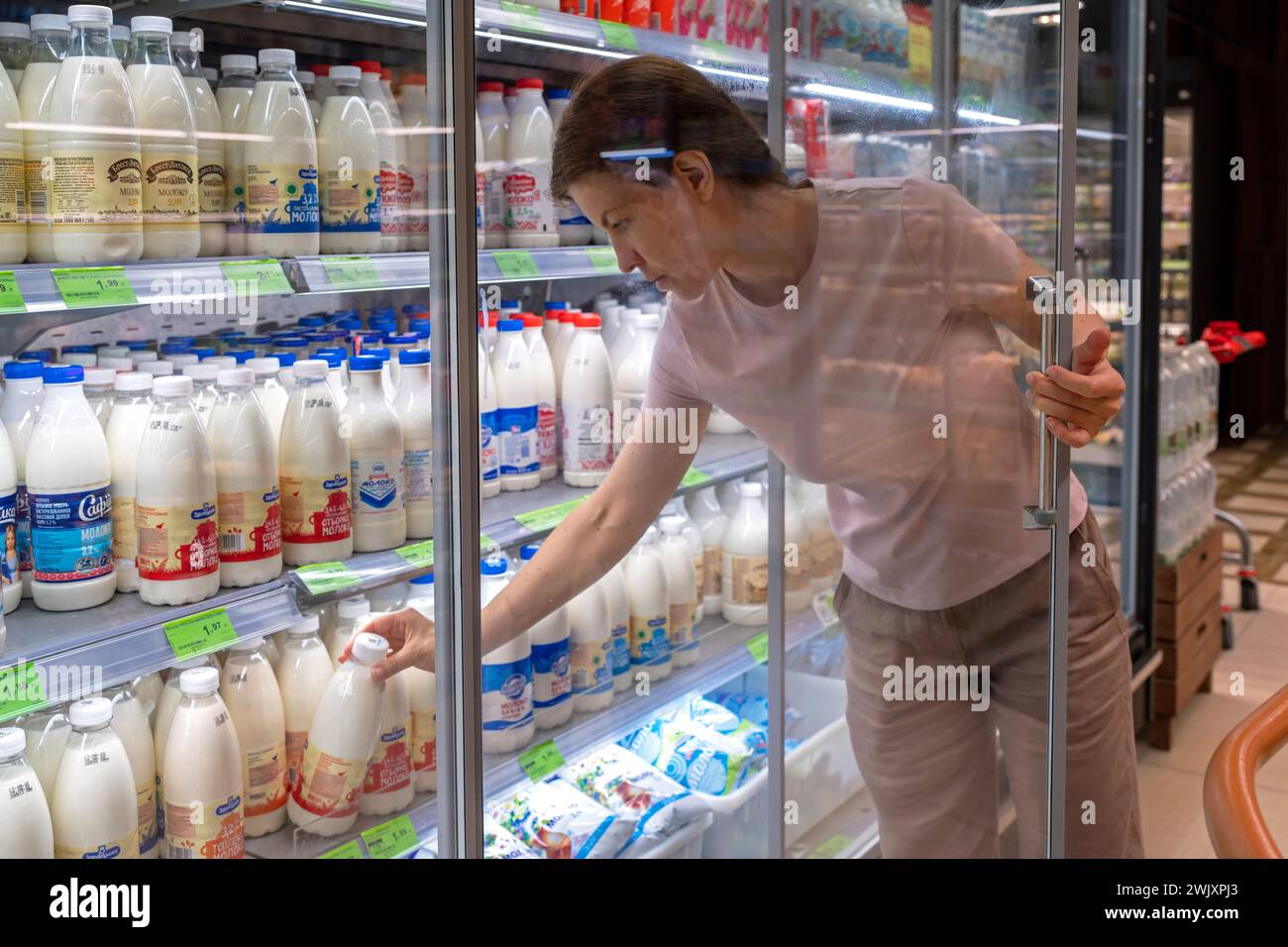 Woman choose dairy produce, take milk and checks expiration date of ...