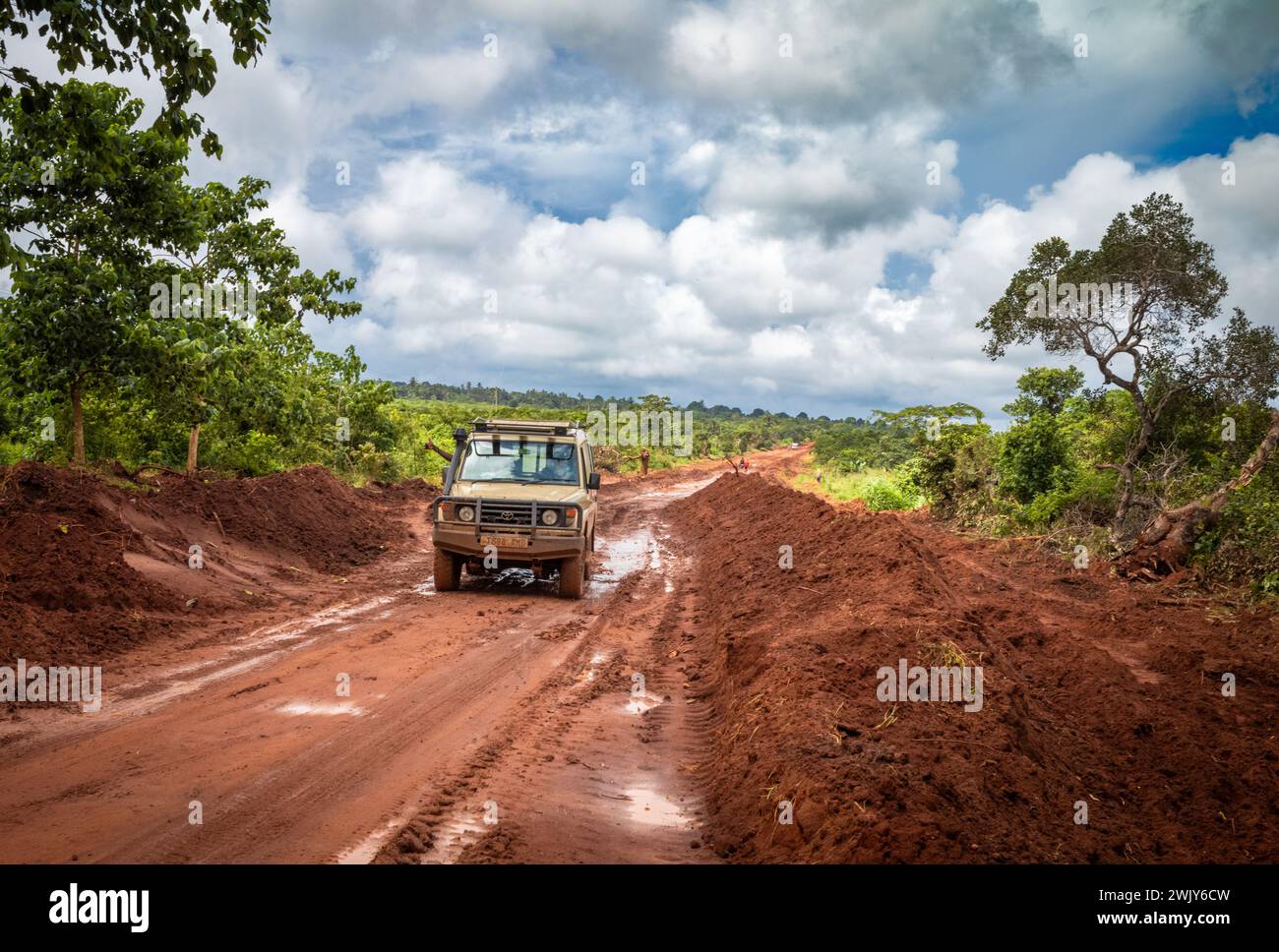 A 4-wheel drive vehicle drives down a wet and muddy red earth road near ...