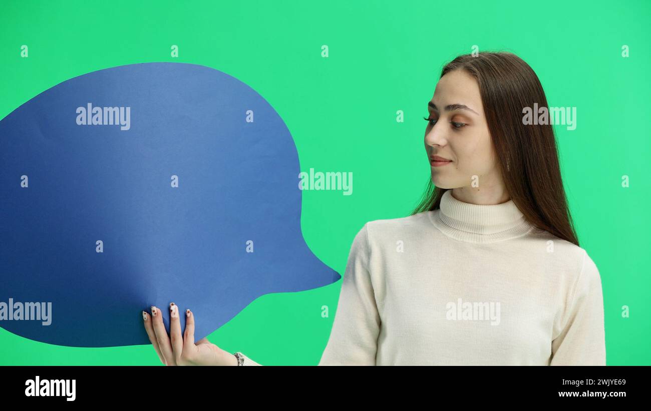 A woman, close-up, on a green background, shows a blue comment sign ...