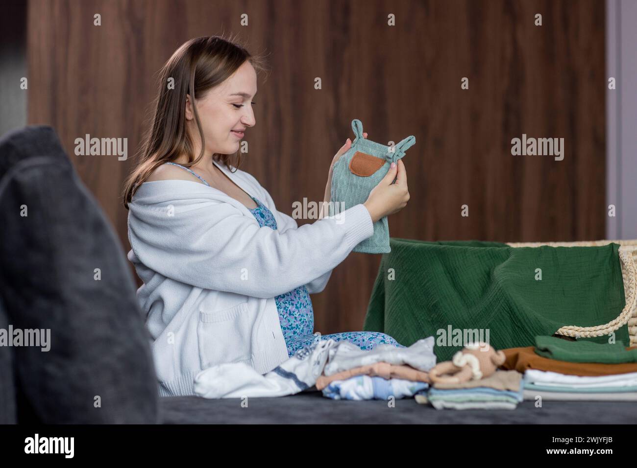 Beautiful pregnant woman looking a cute baby clothes at home ...