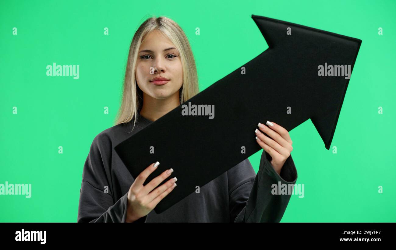 A woman, in close-up, on a green background, points an arrow to the ...