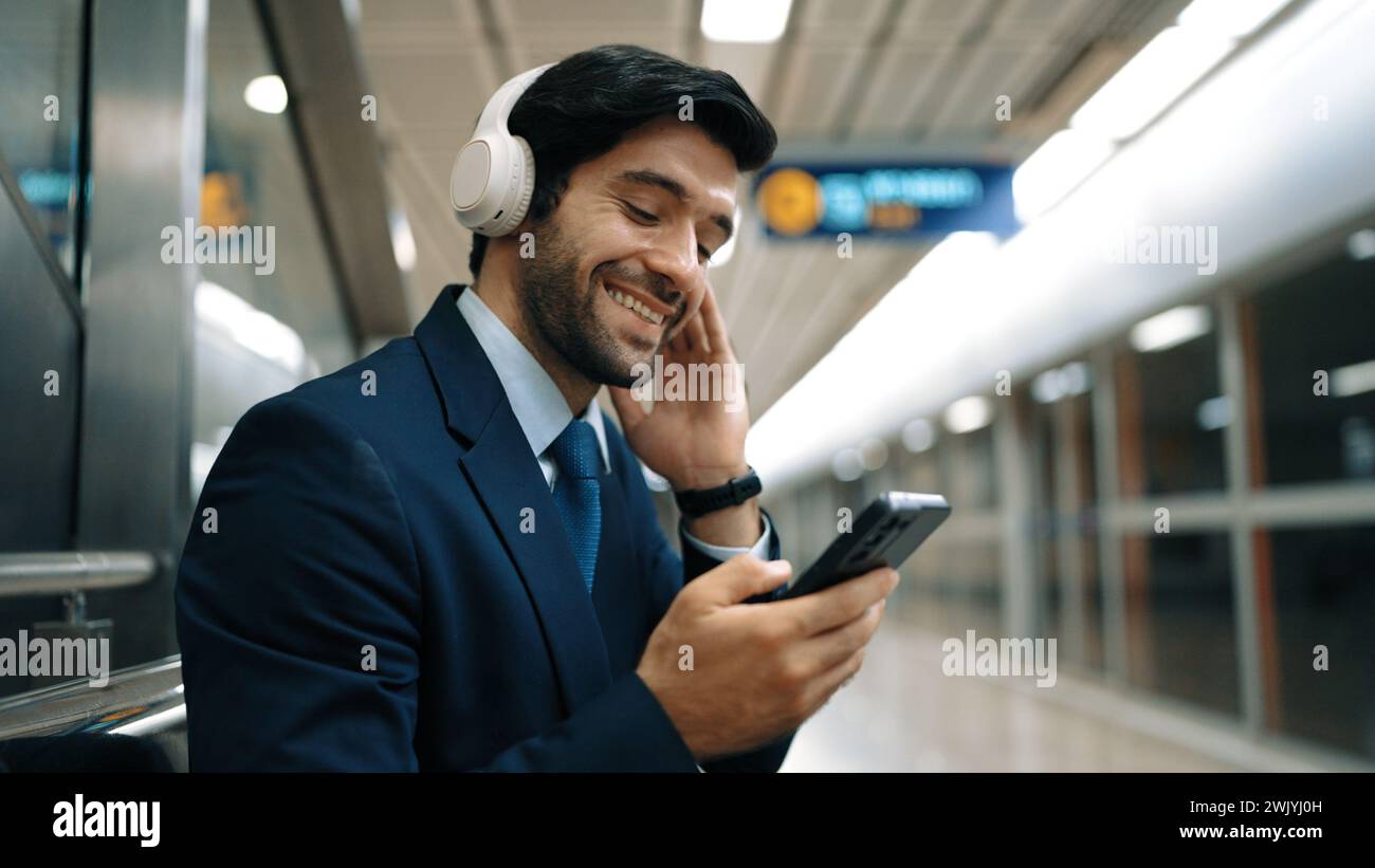 Smart business man listening music by headphone while waiting train at ...