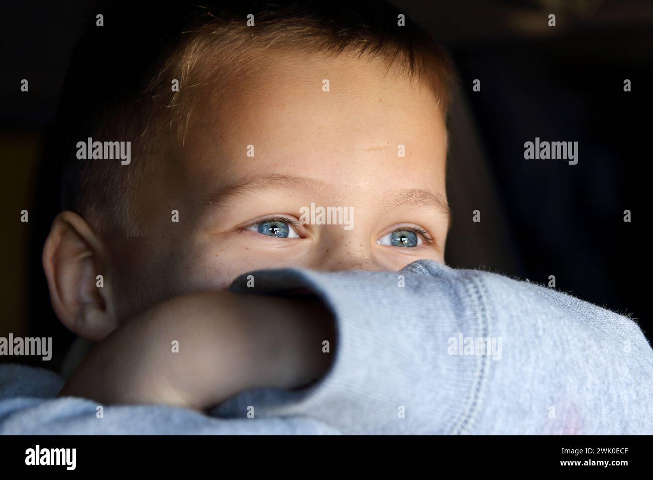 Close up of young boy with deep blue smiling eyes starring off into the ...