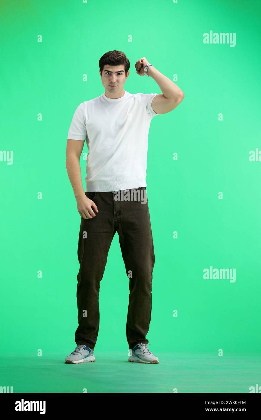 A man in full height, on a green background, raised his hand up Stock ...