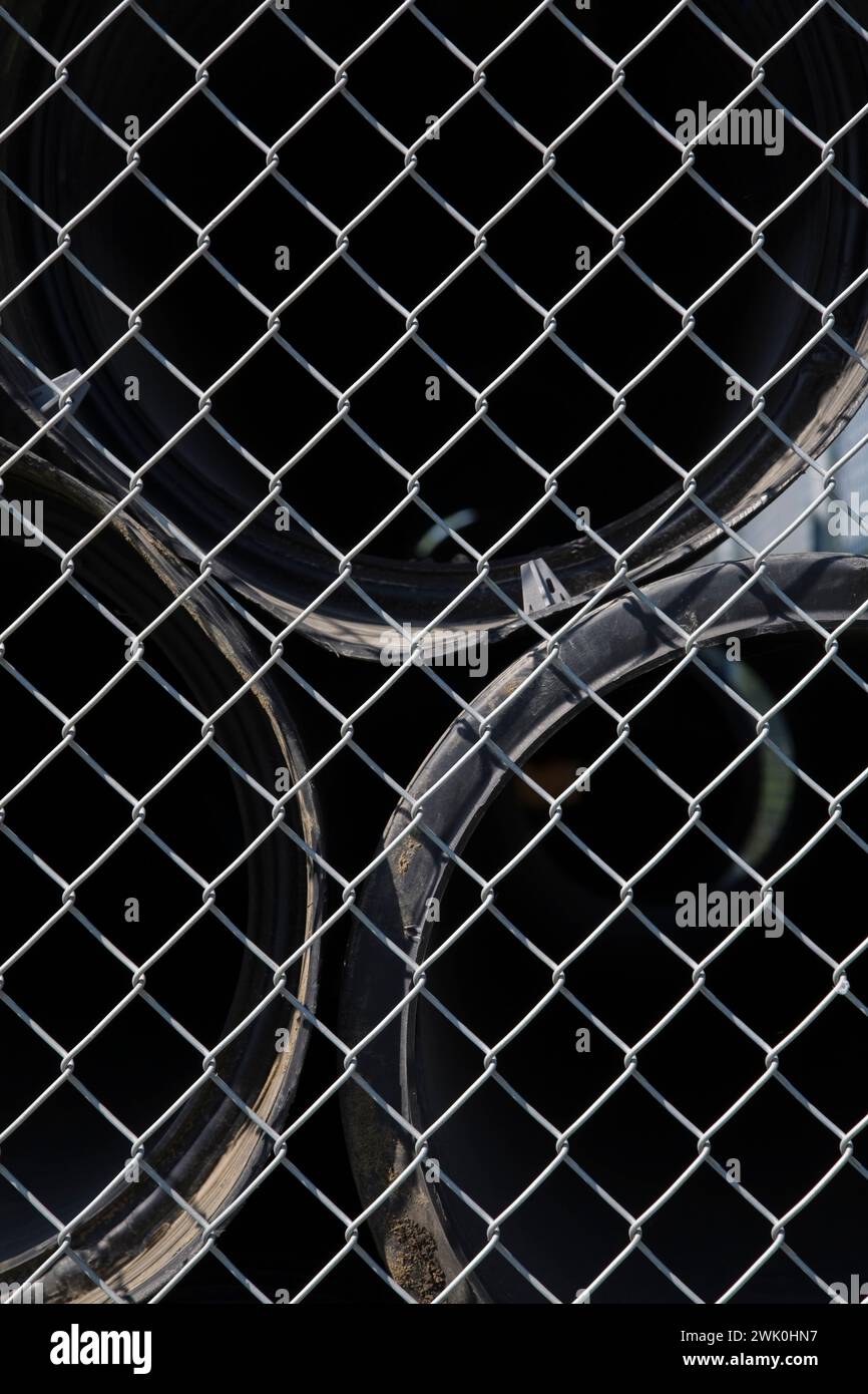 Large black plastic pipes behind steel wire mesh security fence Stock ...