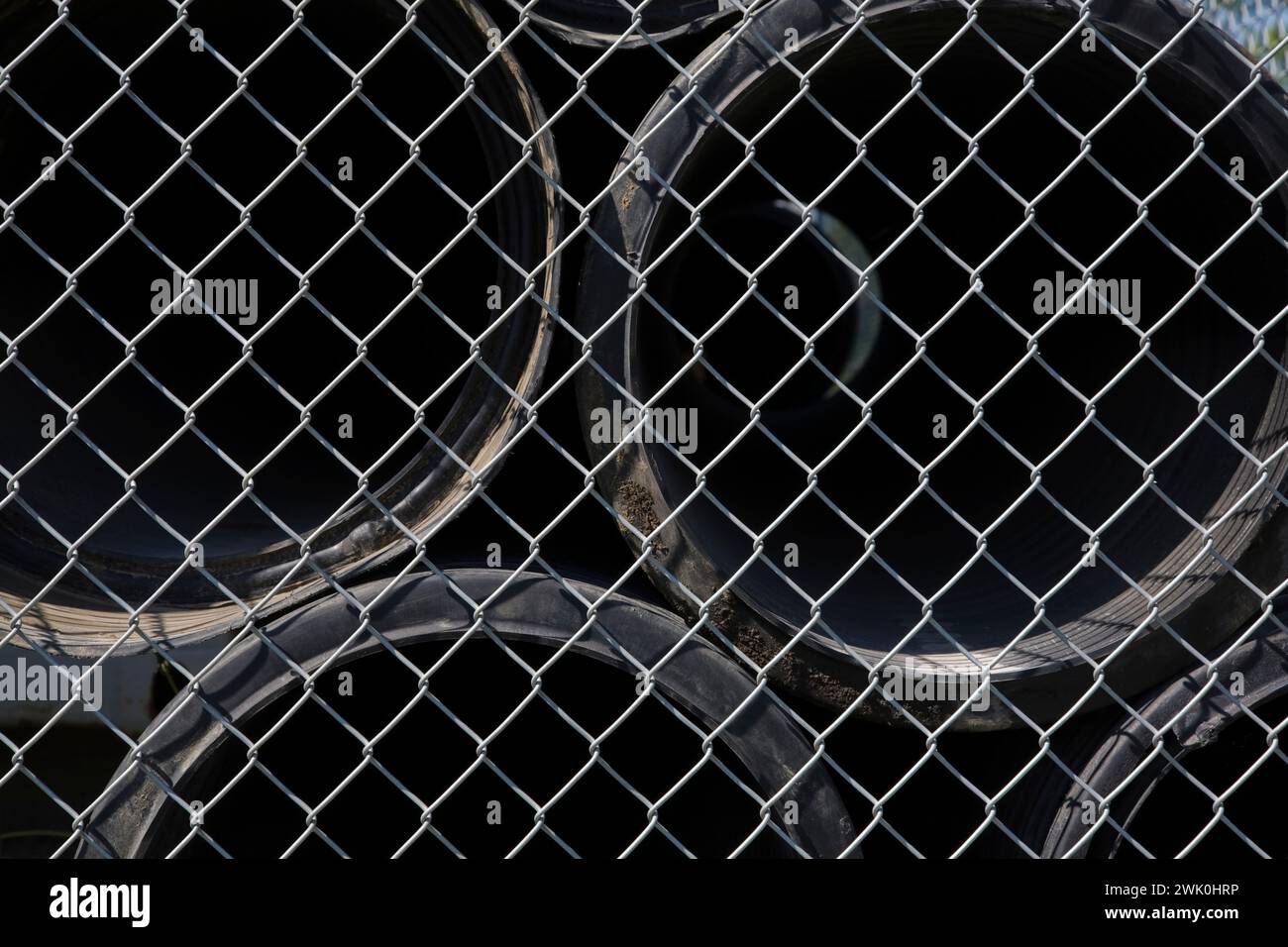 Large black plastic pipes behind steel wire mesh security fence Stock ...