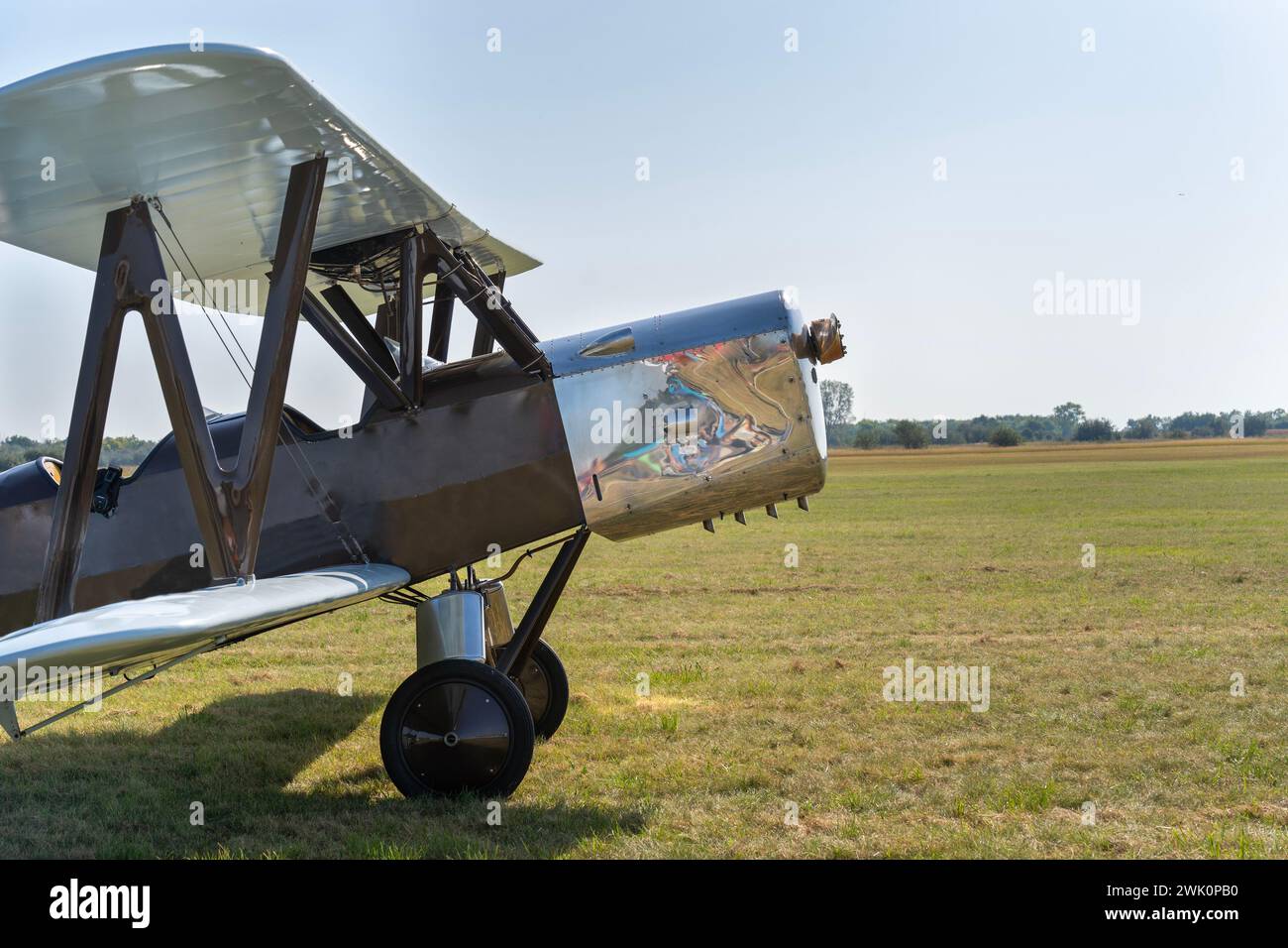 An old brown biplane with a silver metal covering on a grassy airfield ...