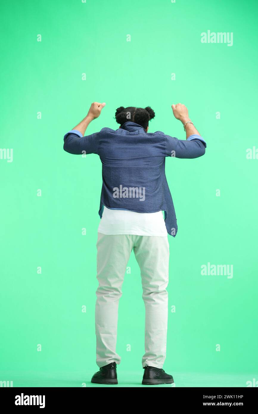 A man, full-length, on a green background, raised his hands up Stock ...