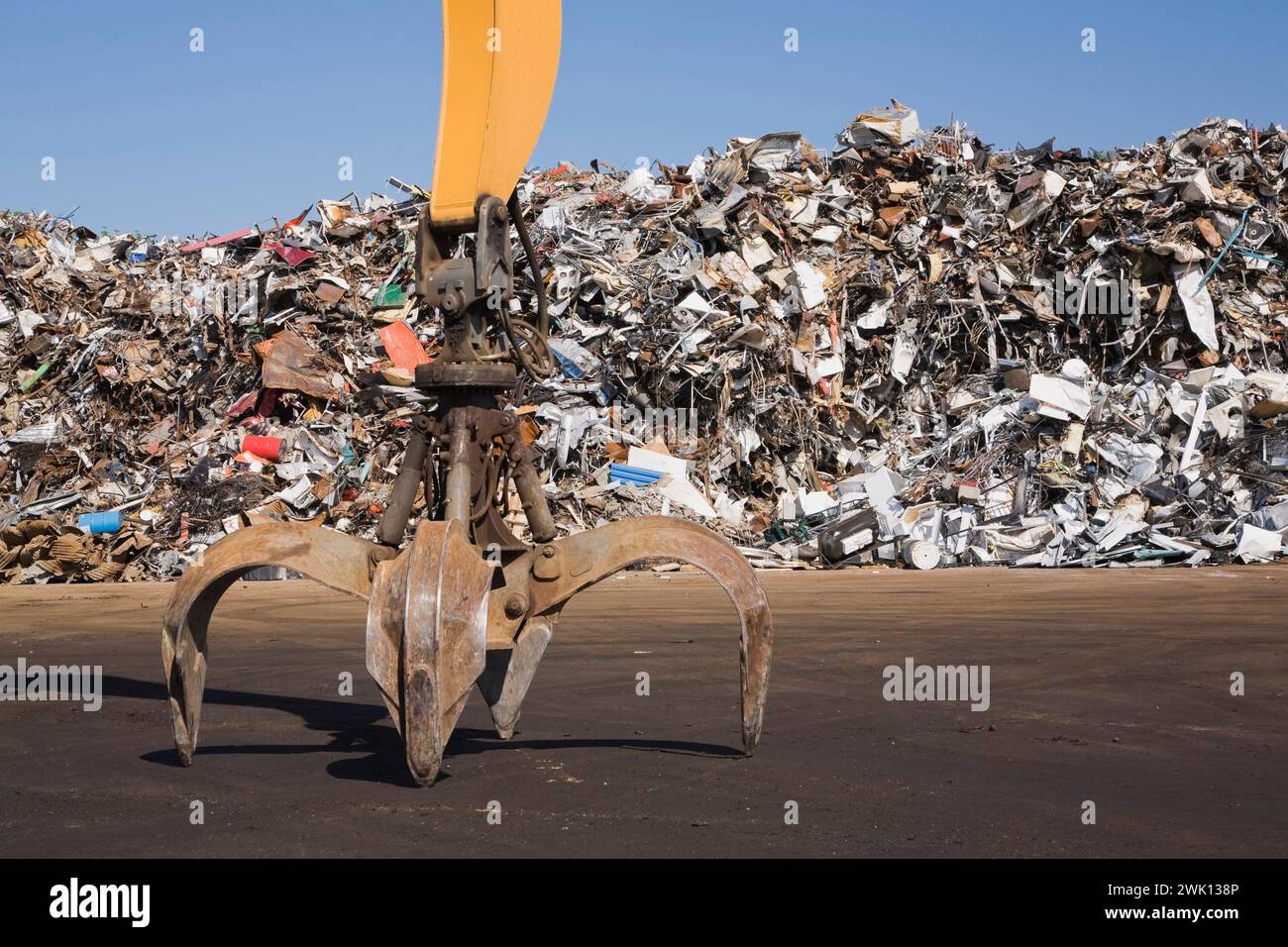 Grappling arm with claw clamp in front of pile of discarded metal ...