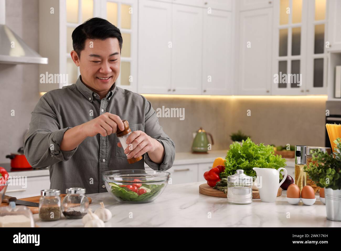 Cooking process. Man adding salt into bowl of salad at countertop in ...