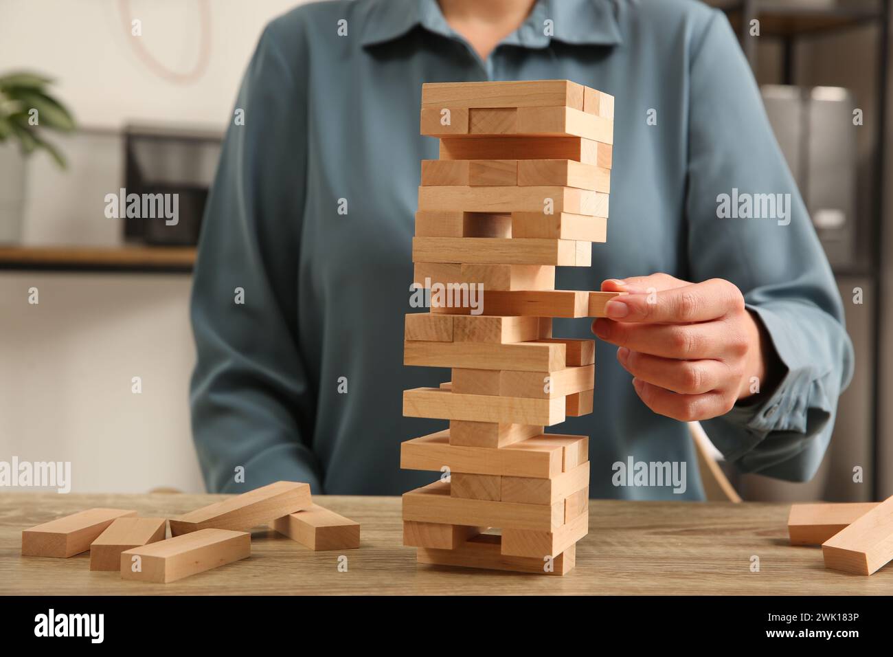 Playing Jenga. Woman removing block from tower at wooden table indoors ...
