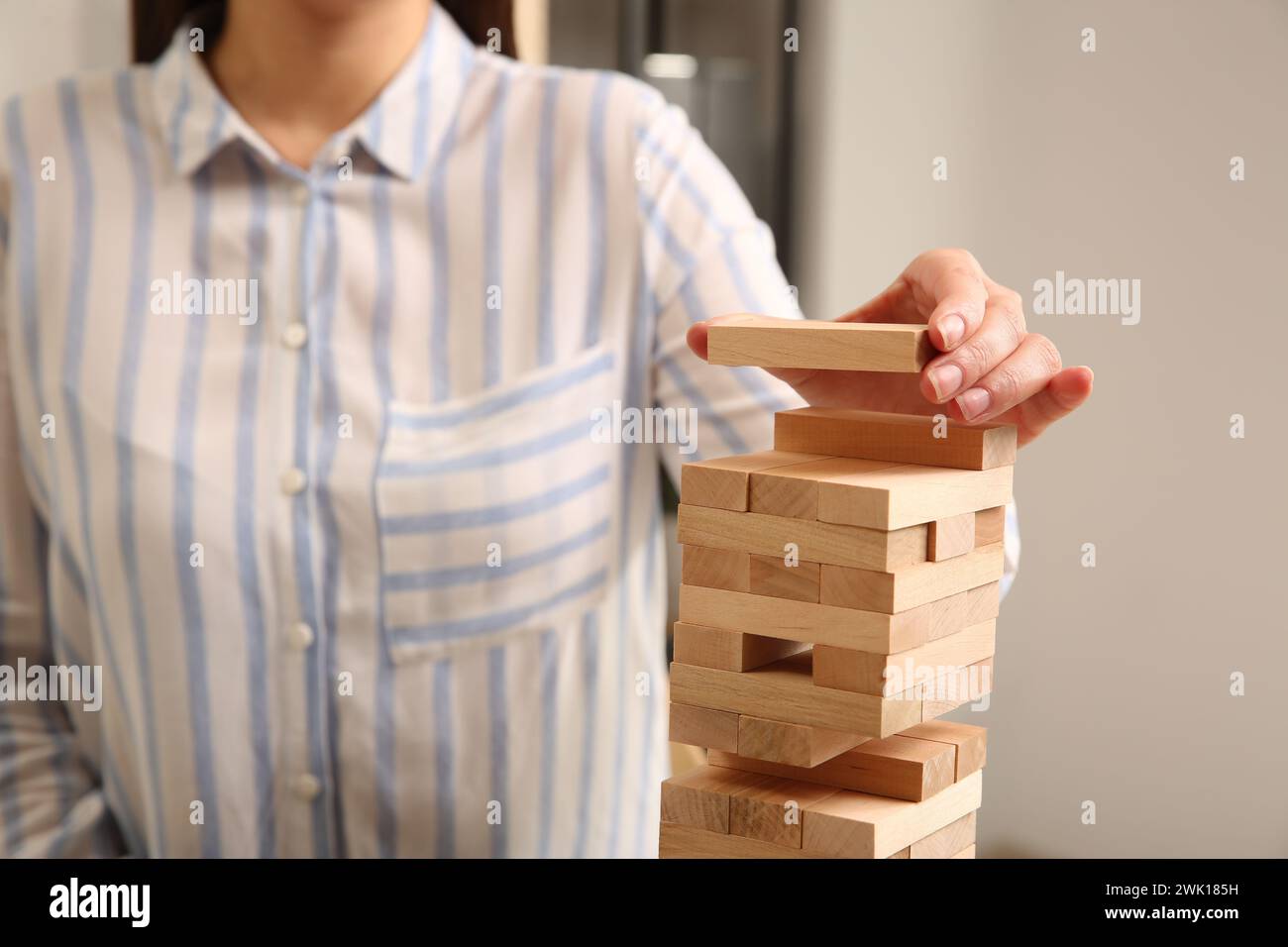 Playing Jenga. Woman building tower with wooden blocks indoors, closeup ...