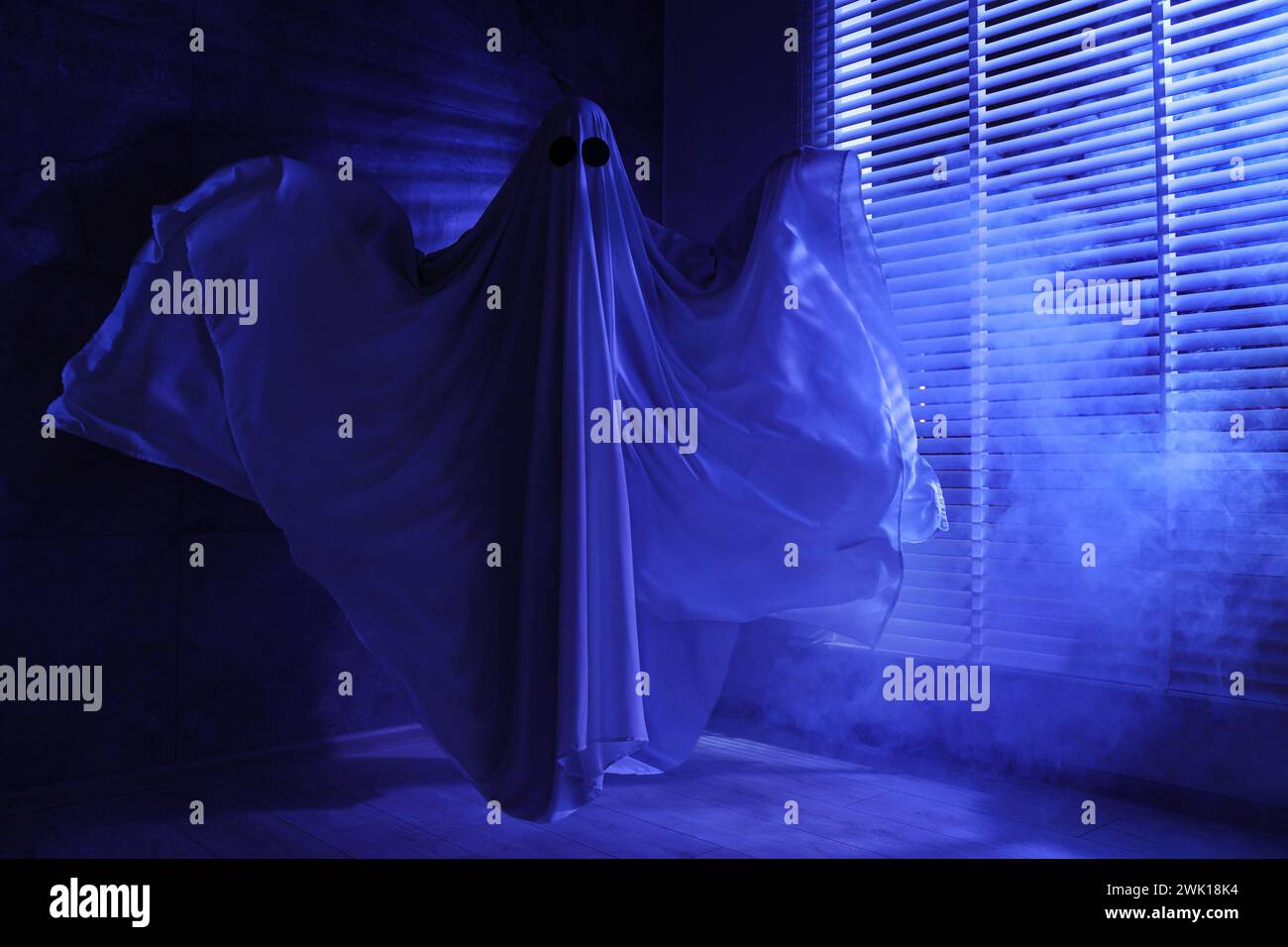 Creepy ghost. Woman covered with sheet near window in blue light Stock ...