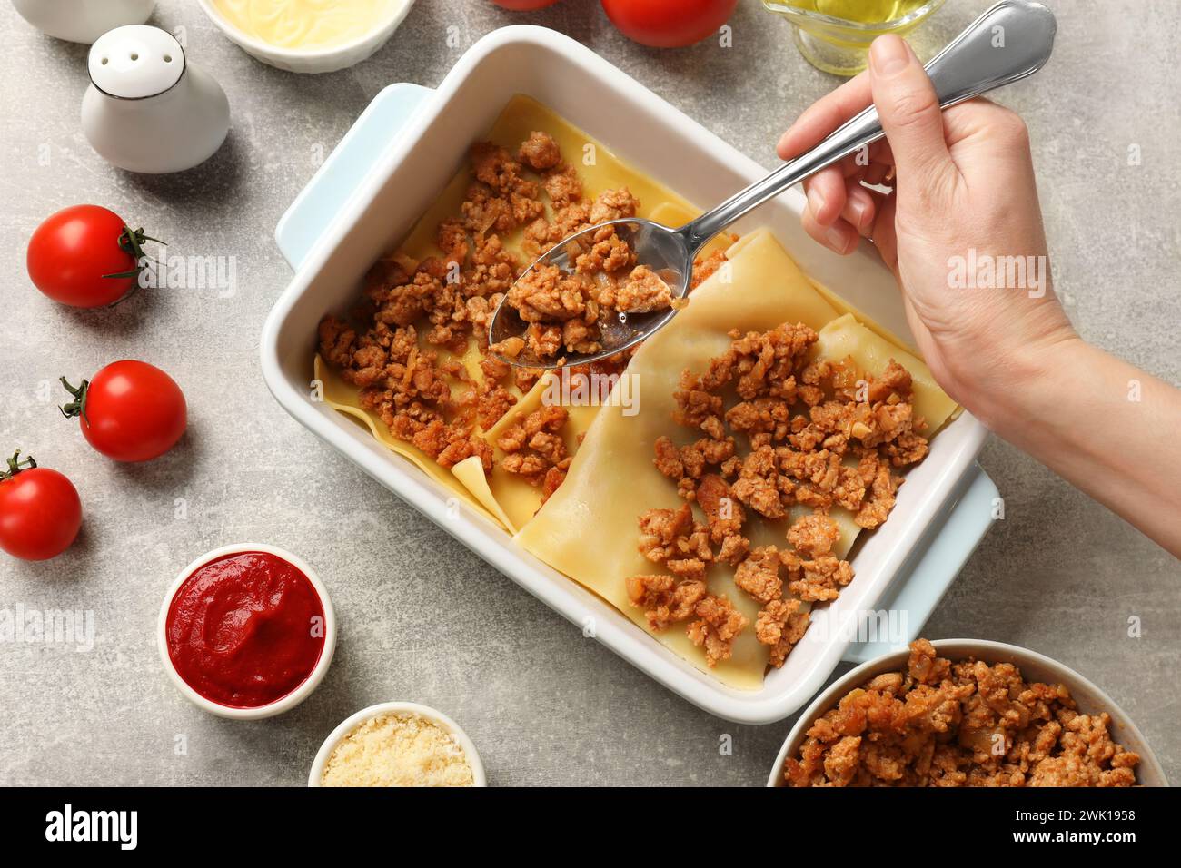 Woman making lasagna at light grey textured table, top view Stock Photo ...